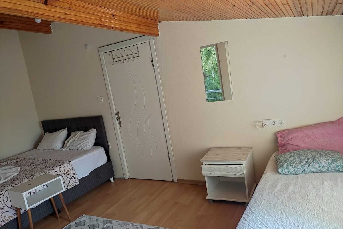 Quarto com cama, mesa de cabeceira, armário e janela com vista para o verde.