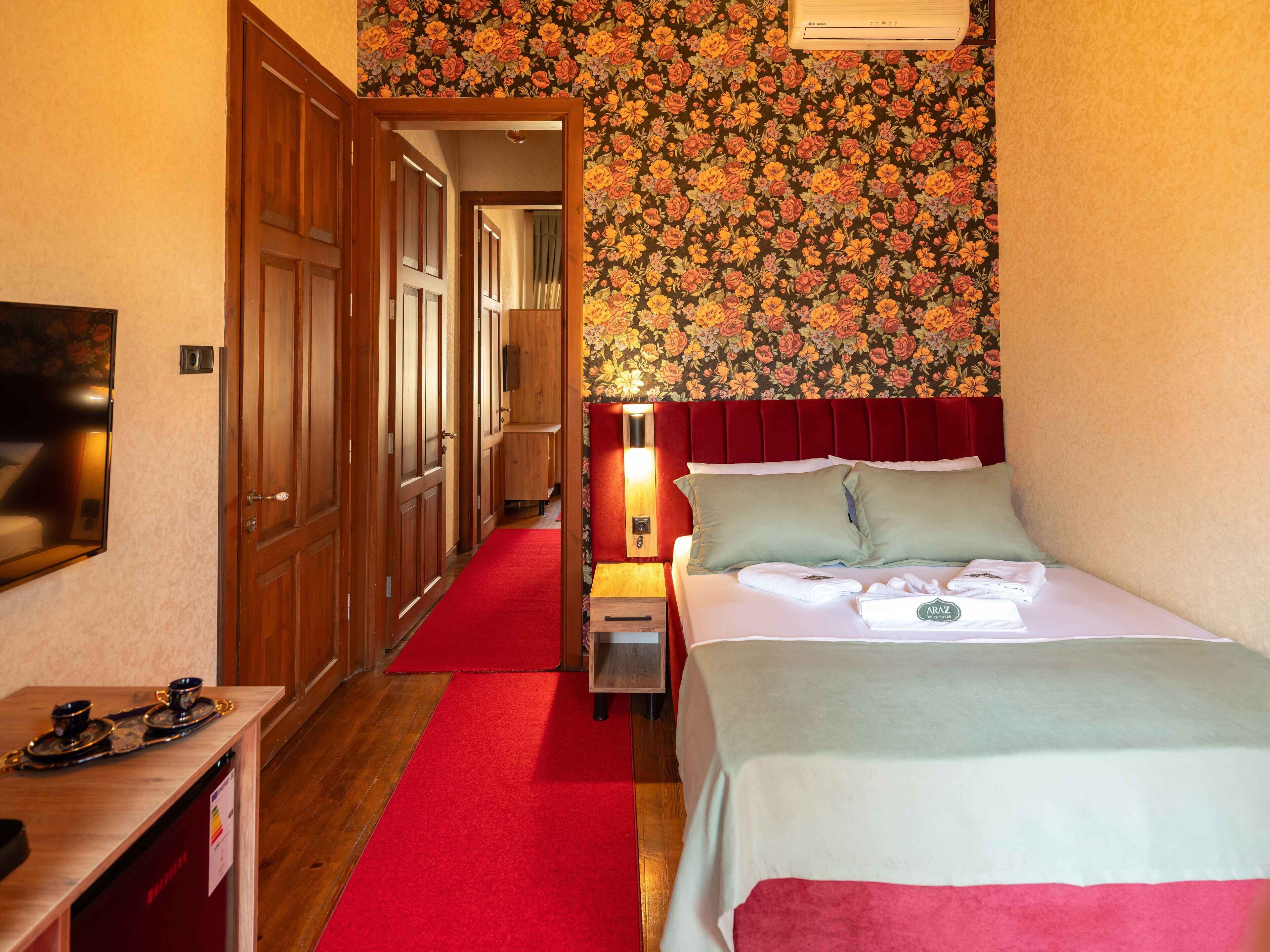 Quarto de hotel com cama, secretária e telefone, e um tapete vermelho.