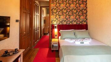 Quarto de hotel com cama, secretária e telefone, e um tapete vermelho.