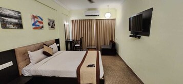 Quarto de hotel com cama, escrivaninha, cadeira, televisão e cortinas.