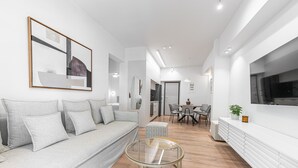 Uma sala de estar moderna com um sofá cinzento, uma mesa de centro de vidro e uma área de jantar com uma mesa e cadeiras brancas.