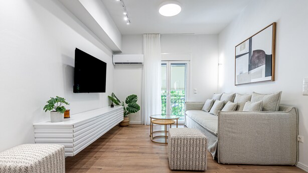 Uma sala de estar moderna com uma televisão de tela plana, um sofá, uma mesa de centro e um aparador com plantas.