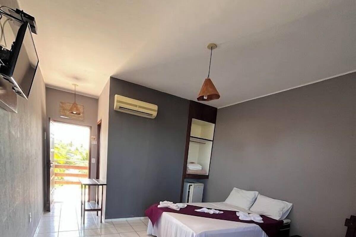 Quarto com duas camas, um banco de madeira, uma televisão, ar condicionado e vista para o exterior.