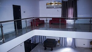 Uma sala de estar espaçosa com guarda-corpo de vidro, um candelabro e um sofá vermelho.