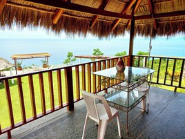 Varanda com mesa e cadeiras de vidro, com vista para uma piscina e um panorama deslumbrante do oceano.