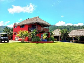Um edifício vermelho com telhado de palha, cercado por um gramado bem cuidado e palmeiras.