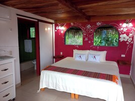 Quarto com cama, penteadeira e janela com vista para o verde.