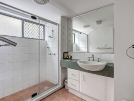 Uma casa de banho moderna com chuveiro em cabine de vidro, uma pia branca e um espelho grande.