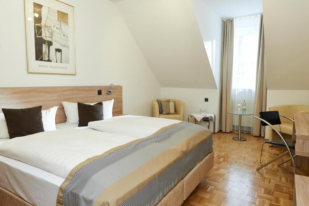 Quarto de hotel com cama grande, mesa pequena, cadeira e janela com cortinas.