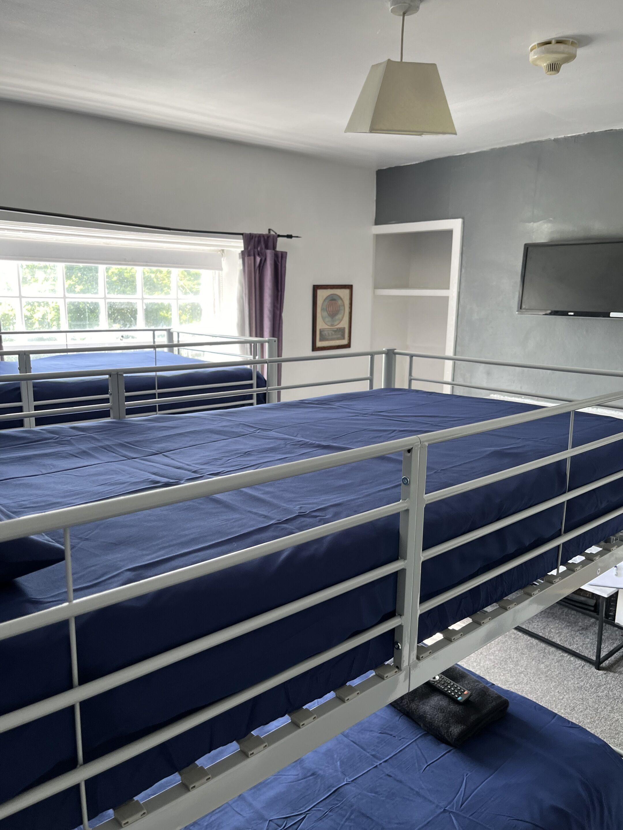 Quarto com beliches, televisão e janela com cortinas.