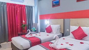 Quarto de hotel com duas camas, roupa de cama vermelha e branca, uma planta em vaso e uma cortina vermelha.