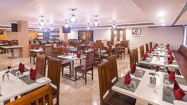 Um restaurante espaçoso com várias mesas e cadeiras, iluminação pendente moderna e uma grande pintura na parede.