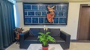 Um saguão com um sofá preto, uma mesa de centro branca, uma planta em vaso e uma janela grande com mosaico.