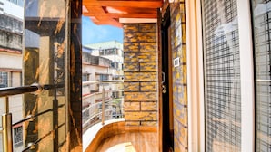 Uma varanda estreita com grade de metal, parede de pedra e vista para edifícios vizinhos.