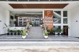 Entrada de um hotel com escadas, plantas em vasos e uma placa com a inscrição 'Hotel Panchwatt Regency'.