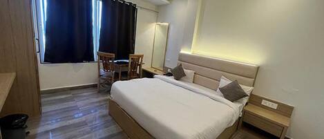Quarto de hotel com uma cama grande, uma escrivaninha, uma cadeira e uma janela com cortinas.