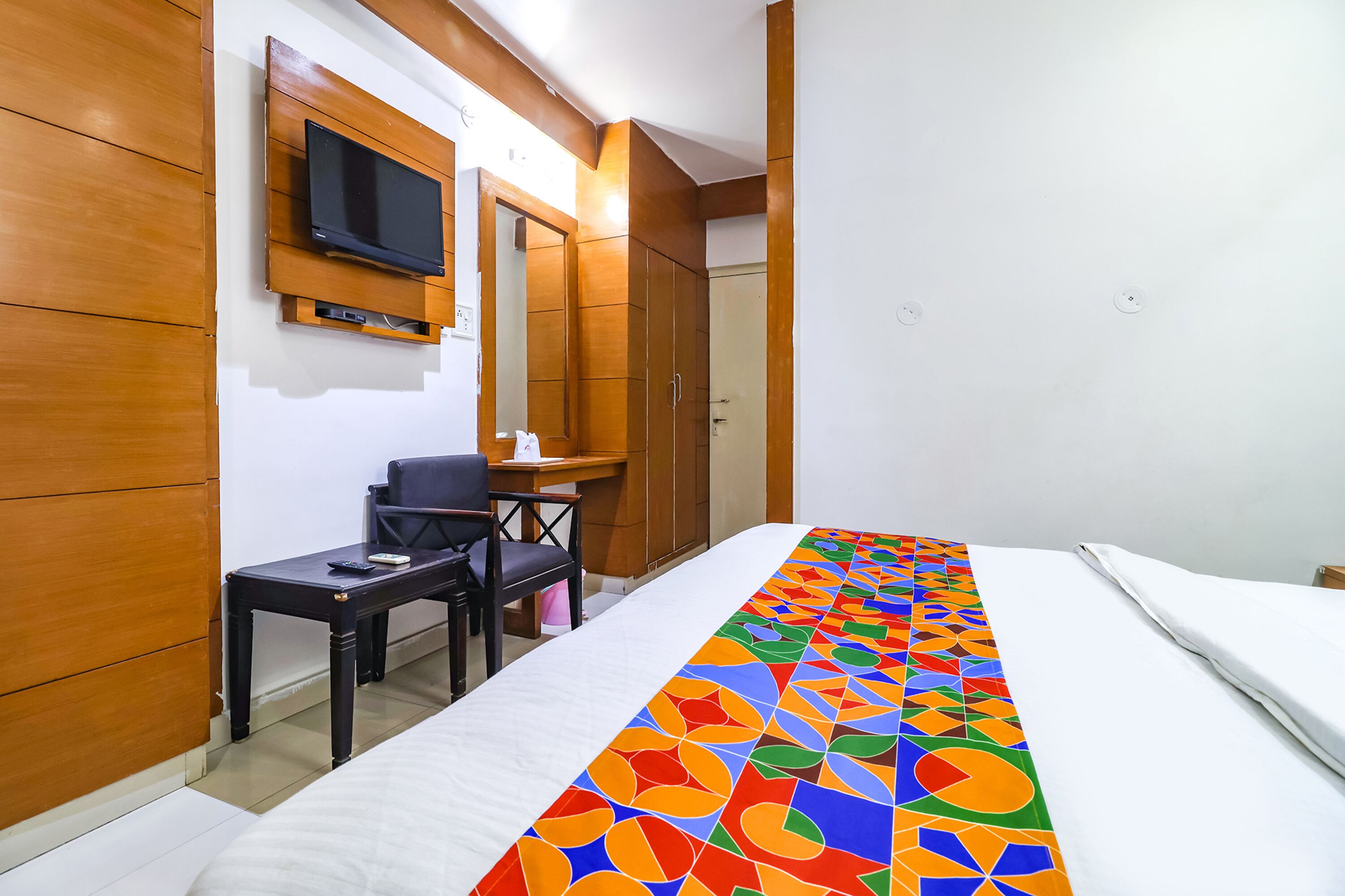 Quarto de hotel com cama, escrivaninha, cadeira, televisão presa à parede e guarda-roupa.