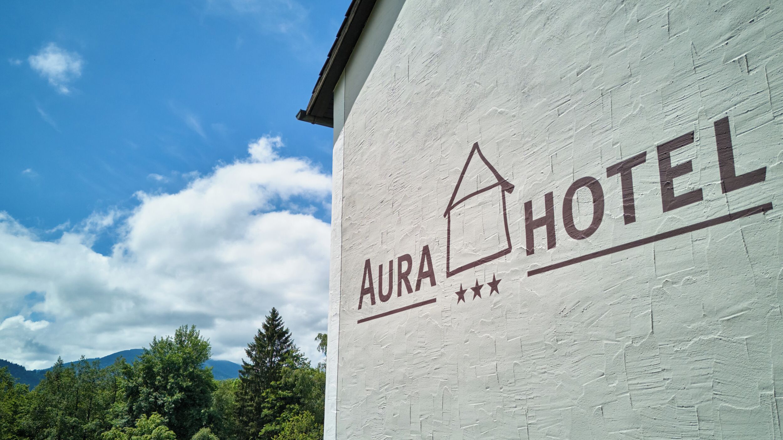 Paredes brancas com o texto "AURA HOTEL" e um ícone de casa, indicando um hotel.
