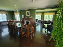 Uma sala de jantar com mesa e cadeiras de madeira, lareira e janelas amplas com cortinas.