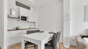 Uma cozinha moderna com armários brancos, micro-ondas e uma mesa de jantar com cadeiras.