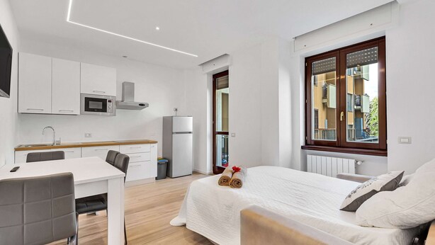 Quarto de hotel moderno e compacto com cozinha compacta, área de refeições e cama com toalhas dobradas.