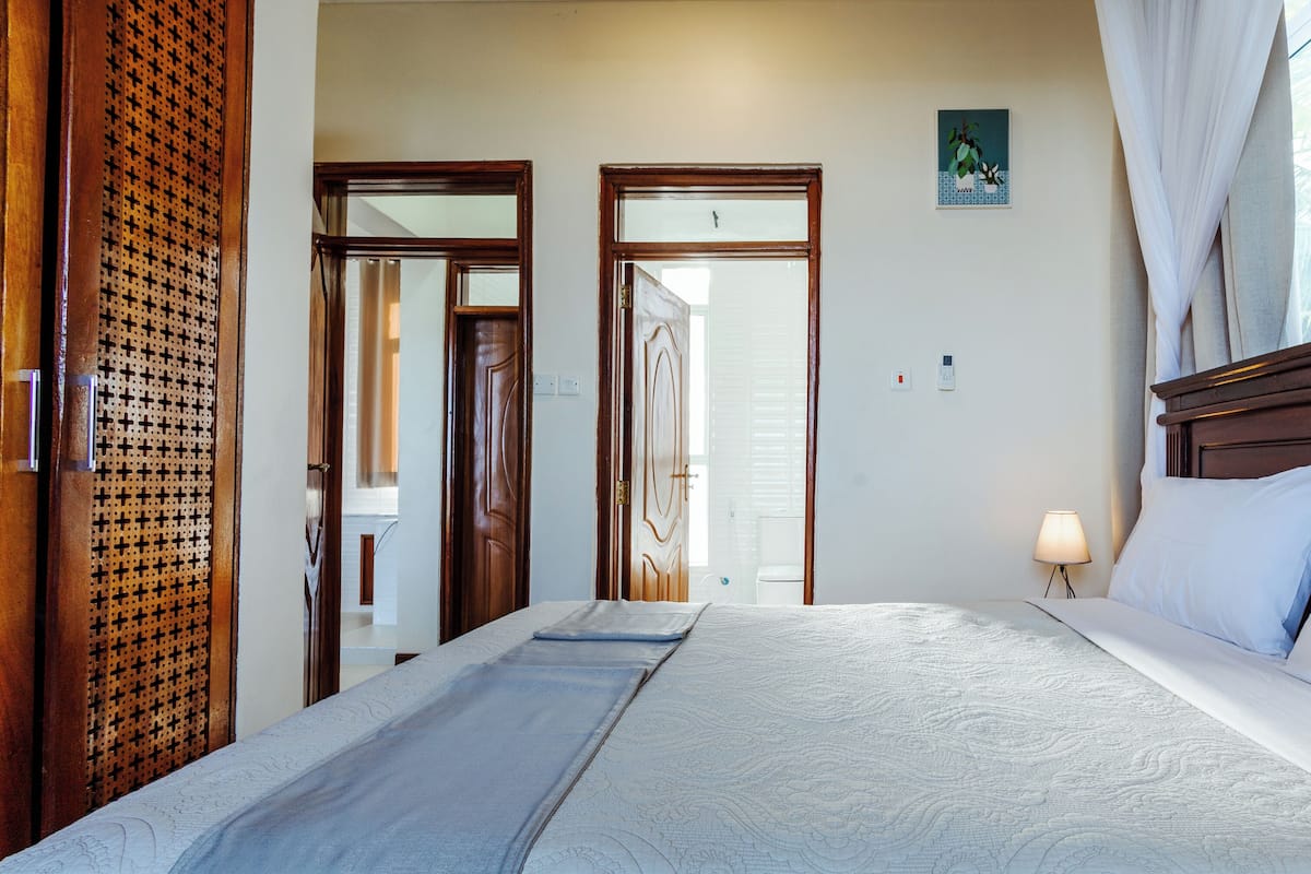 Quarto de hotel com uma cama grande, cabeceira de madeira e vista para o banheiro por uma porta aberta.