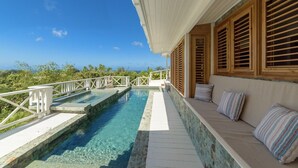 Uma área de piscina com deck de madeira, guarda-corpo branco e espaço para sentar com almofadas.