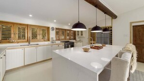 Cozinha moderna com armários brancos, uma ilha grande, iluminação pendente e uma viga de madeira rústica.