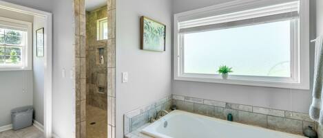 Uma casa de banho moderna com uma banheira grande, zona de duche e janela com vista.