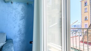 Quarto com parede azul, sofá azul, porta de vidro que dá para o exterior e vista de um edifício na rua.