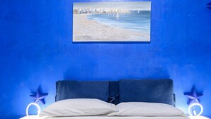 Quarto com cama, parede azul e pintura de uma cena de praia.