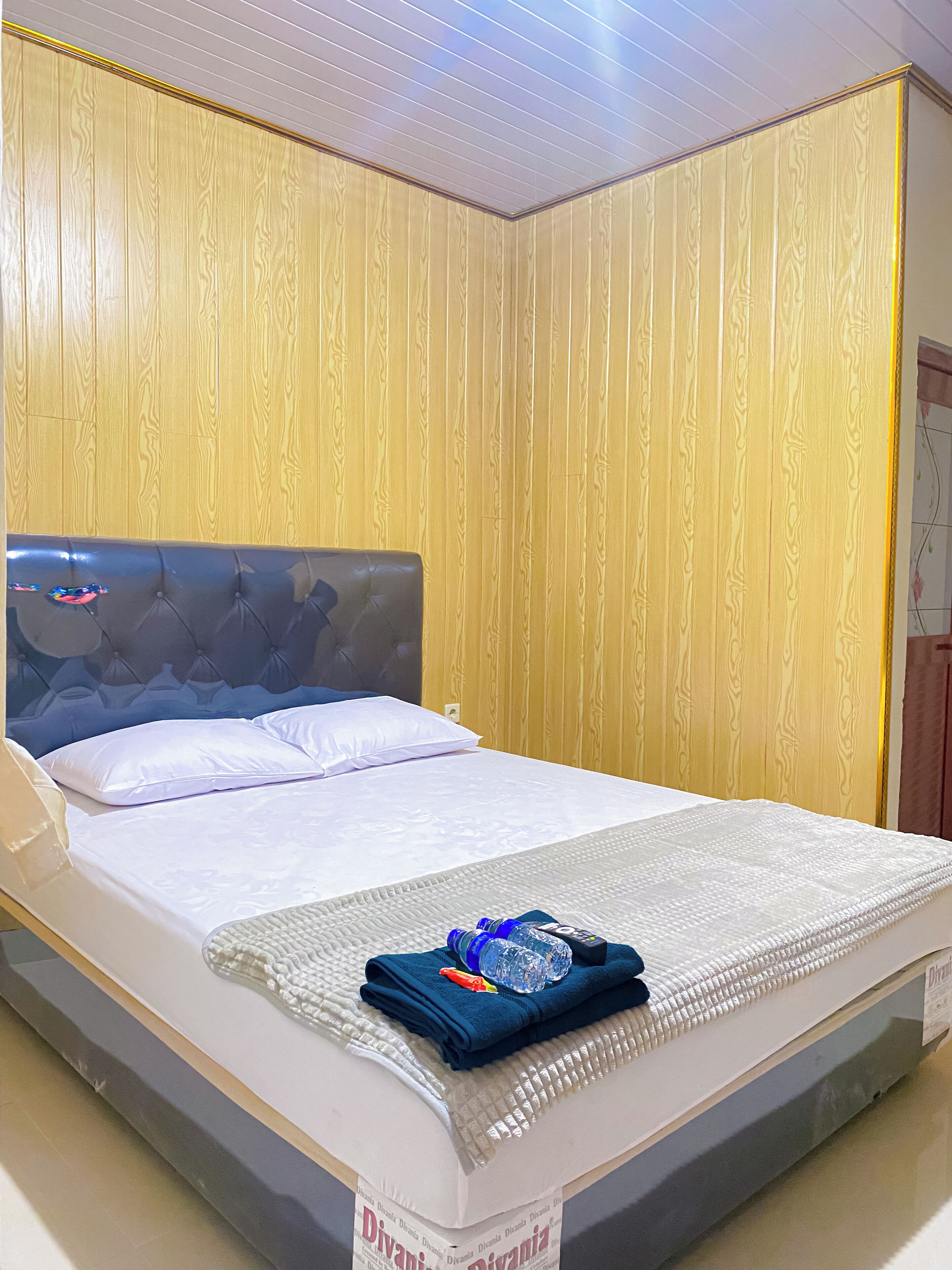 Quarto de hotel com cama, cabeceira, colchão, travesseiros, cobertor e uma garrafa de água.