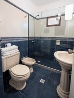 Casa de banho com sanita, bidé e lavatório, com azulejos azuis e cabine de duche em vidro.