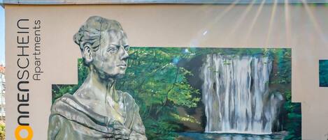 Um mural com uma estátua clássica e uma cascata na fachada de um edifício.