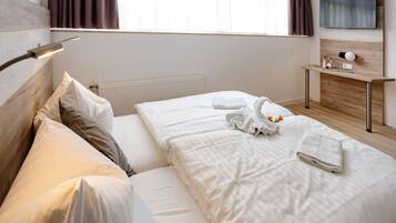 Quarto de hotel com cama, mesa de cabeceira com abajur, televisão e janela com cortinas.