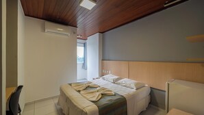 Quarto de hotel com cama, escrivaninha, cadeira e janela.