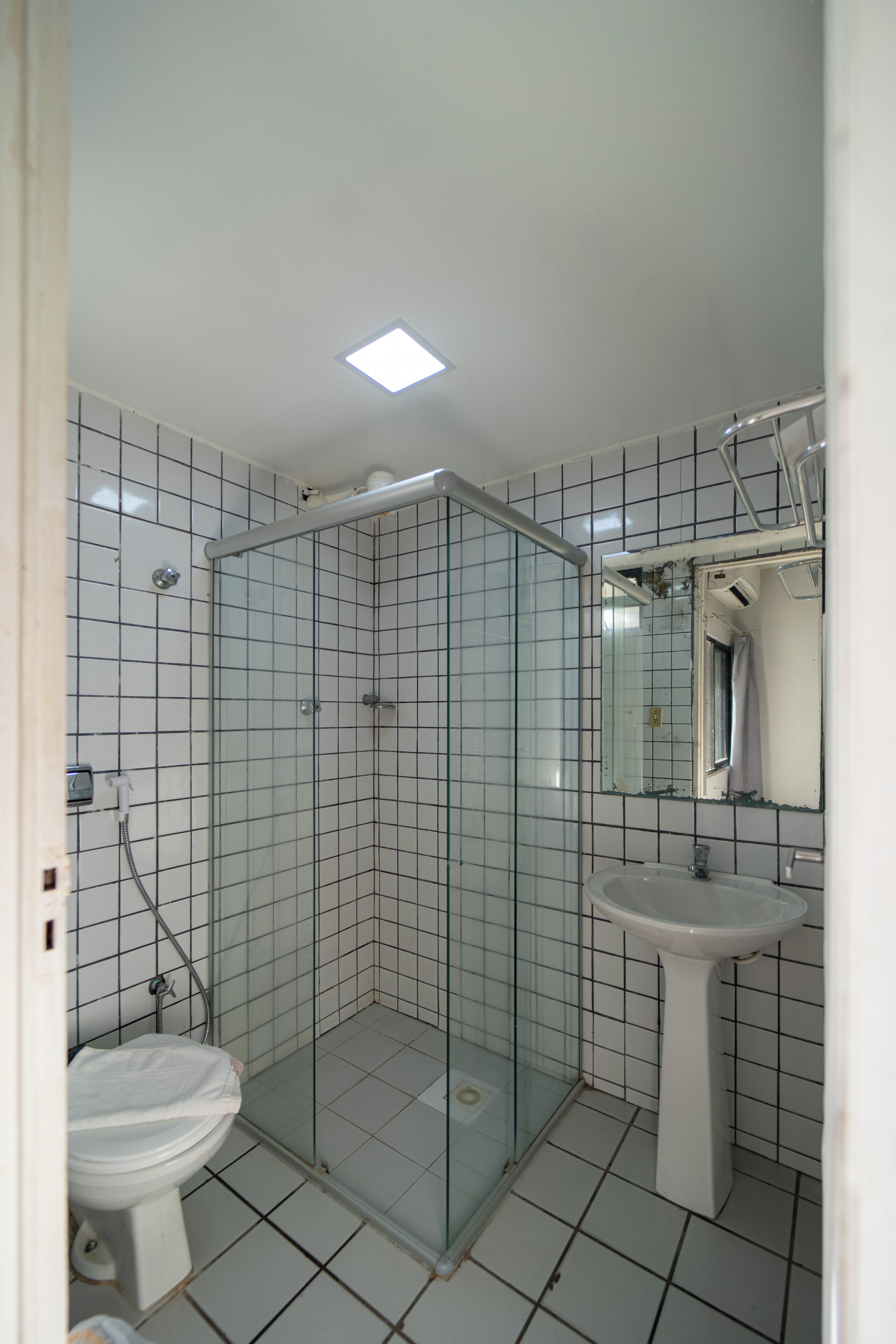 Casa de banho com cabine de duche em vidro, lavatório branco e sanita.