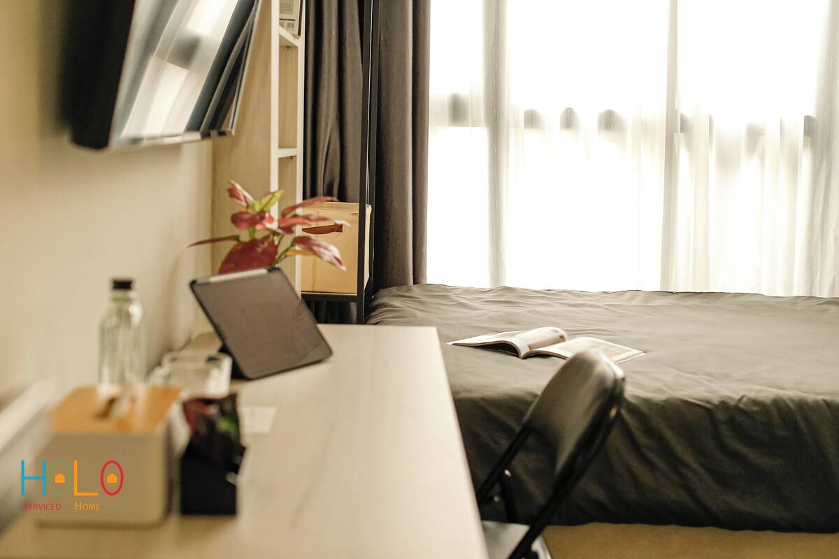 Quarto de hotel com uma cama, uma escrivaninha com um laptop, uma garrafa, uma caixa de lenços e uma planta em vaso.