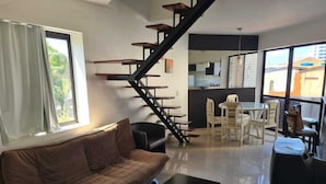 Uma sala de estar moderna com um sofá marrom, uma mesa de centro preta e uma escada que dá para uma área de cozinha.