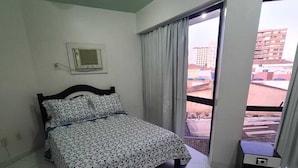 Quarto com cama, janela e vista para prédios.