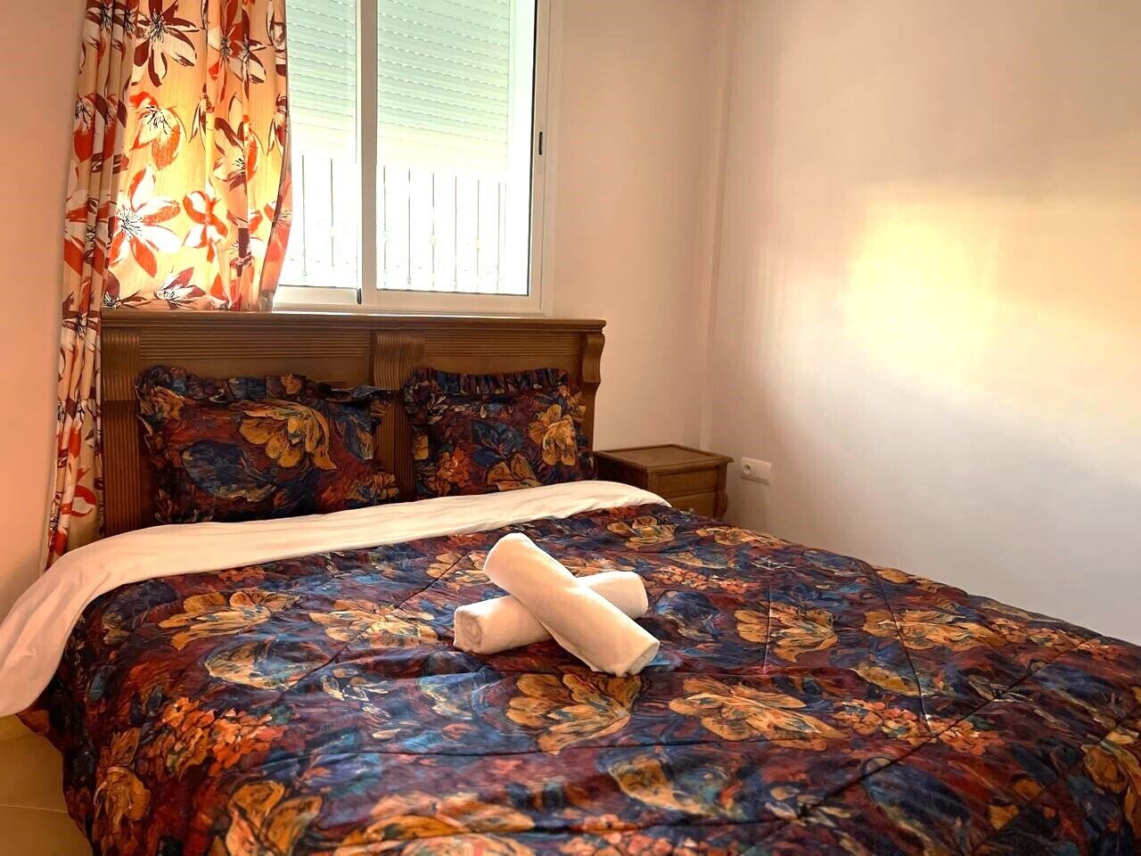 Cama com colcha florida, duas almofadas e toalhas enroladas.