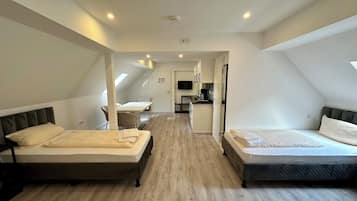 Quarto moderno e bem iluminado com duas camas, uma kitchenette e um pequeno espaço para refeições.
