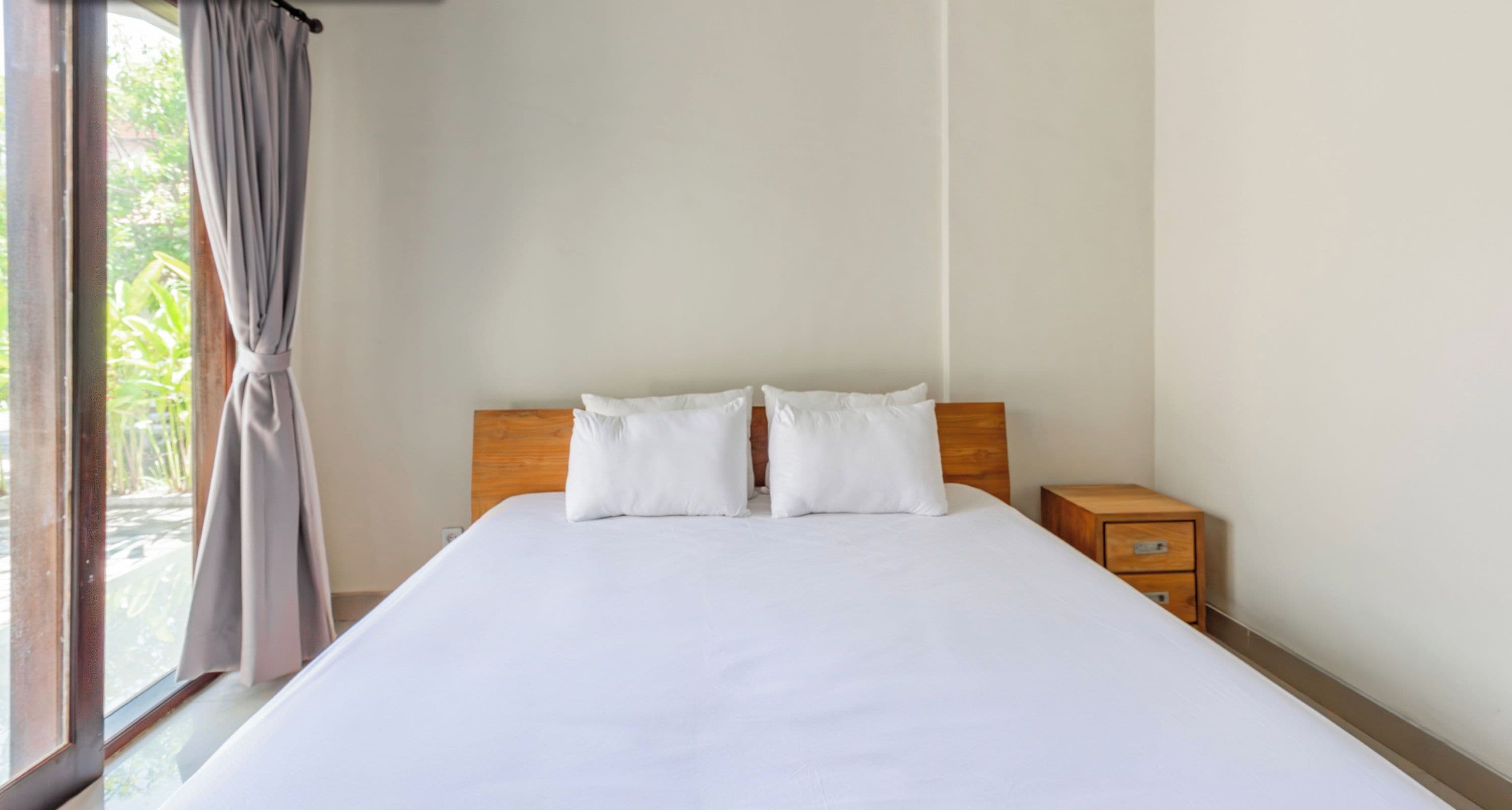 Uma cama bem arrumada com roupa de cama branca, uma cabeceira de madeira e uma pequena mesa de cabeceira de madeira com uma gaveta.