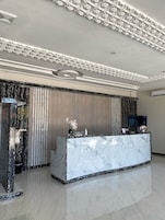 Uma área de recepção moderna com balcão de mármore, teto decorativo e uma grande janela com cortinas.