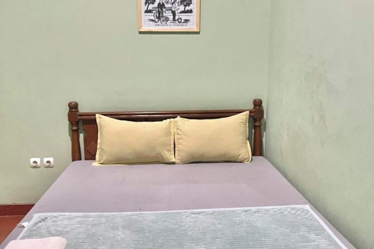 Uma cama com cabeceira de madeira, um travesseiro amarelo e um edredom cinza.