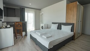 Quarto de hotel moderno com uma cama grande, escrivaninha com chaleira, máquina de lavar e guarda-roupa.
