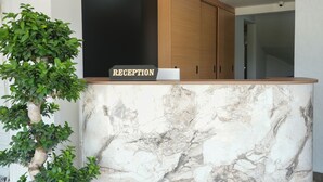 Uma receção com bancada de mármore, um letreiro a dizer "RECEPTION" e uma planta em vaso à esquerda.