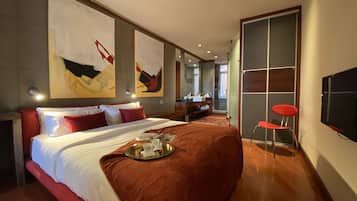 Quarto de hotel moderno com uma cama grande, televisão, banheiro e obras de arte nas paredes.