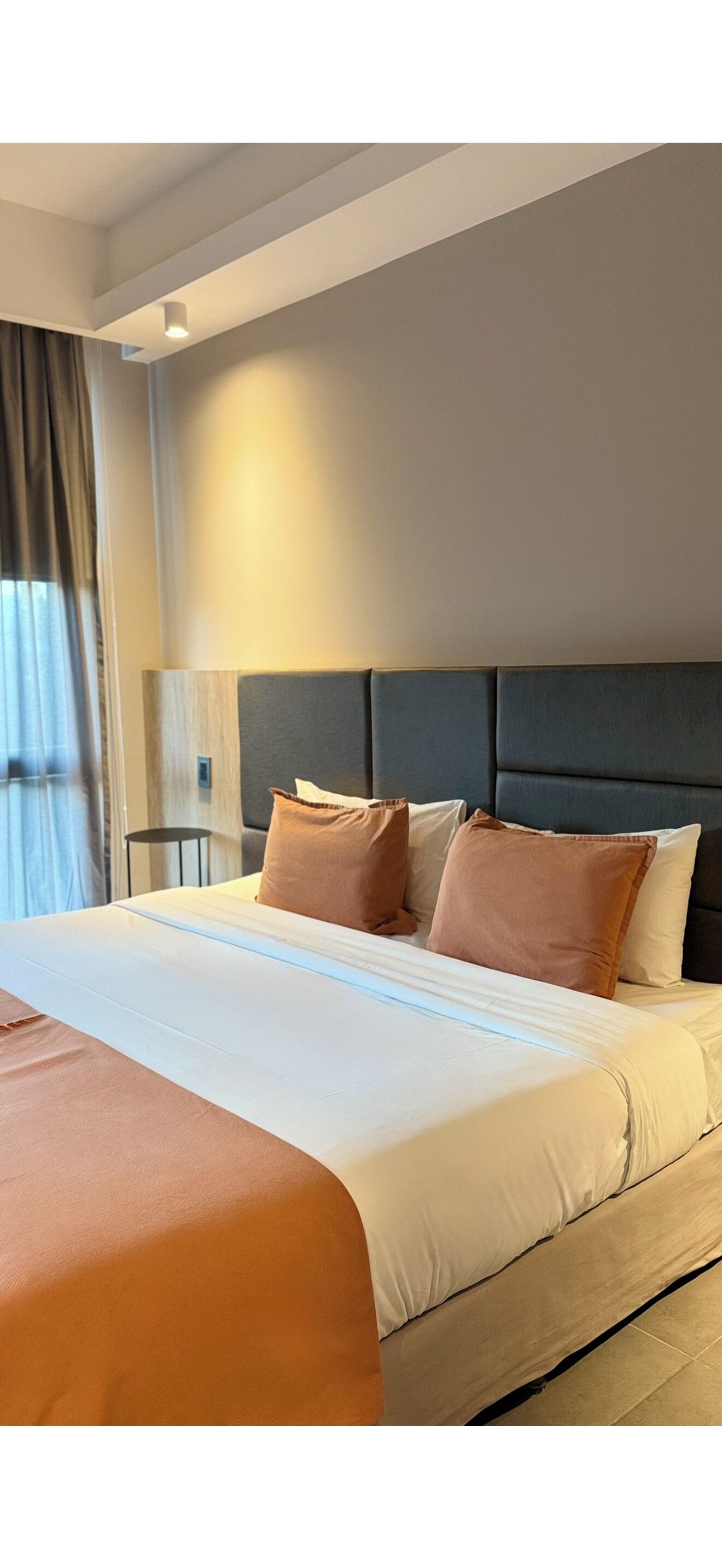 Quarto de hotel moderno com uma cama grande, cabeceira e mesa de cabeceira.