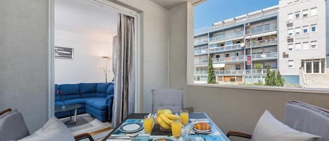 Uma varanda com uma mesa de jantar posta para o café da manhã, um sofá azul e vista para um prédio residencial.
